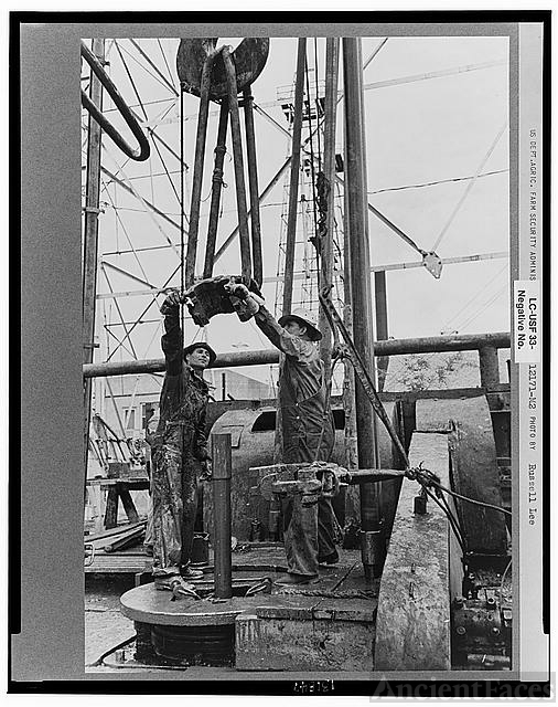 Oil field workers, reaching for clamp on elevator. The...